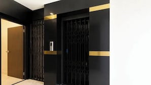 Um corredor com uma porta preta, um portão preto e um pequeno dispositivo eletrônico na parede.