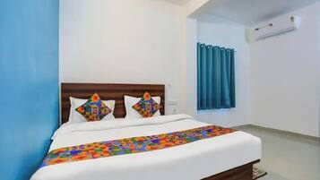 Quarto de hotel com cama, cabeceira, janela com cortinas e aparelho de ar condicionado.