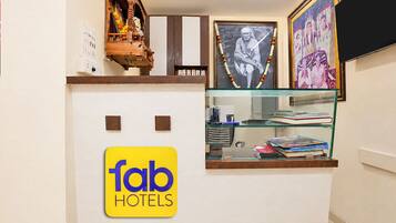 Uma área de recepção de hotel com uma placa para 'fab hotels', um armário de madeira com objetos, fotografias emolduradas e uma vitrine de vidro com livros.