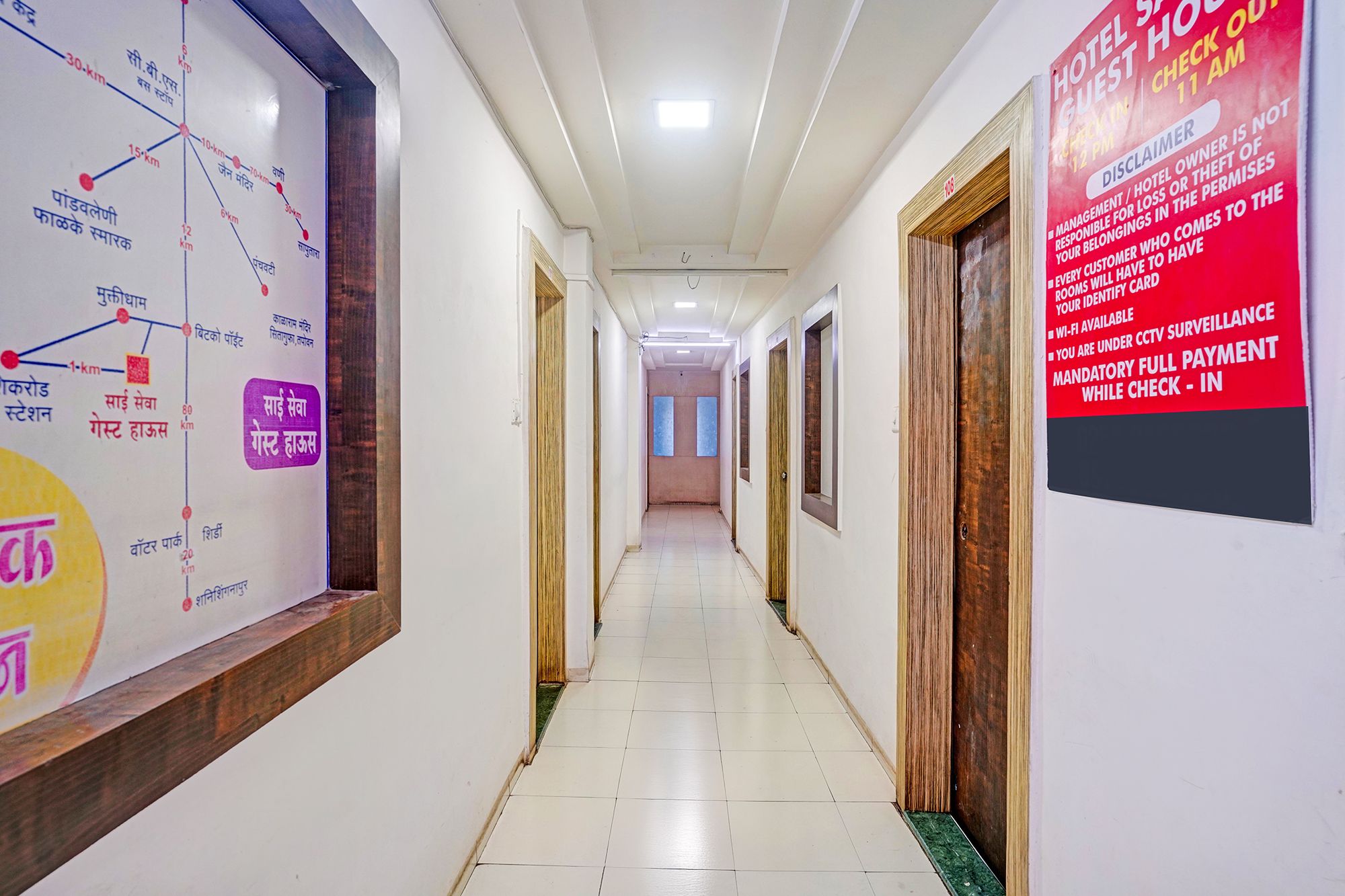 Corredor de hotel com um mapa na parede esquerda, um aviso de check-in na parede direita e piso de azulejos.