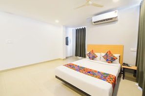 Quarto de hotel com cama, ventilador de teto, ar condicionado e mesa de cabeceira com telefone.