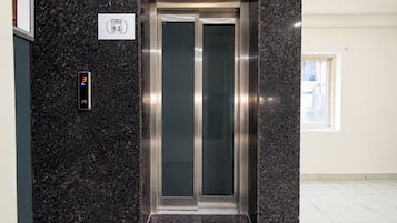 Um elevador com visor digital, sinal indicando limite de tempo para uso e porta com painel de vidro jateado.