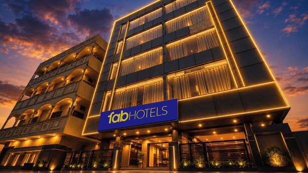 Um hotel moderno com um destaque para a placa 'fabHOTELS', várias varandas e fachada bem iluminada.