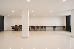 Quarto amplo com teto alto, iluminação embutida, um pilar central e uma fileira de cadeiras ao longo de uma parede.