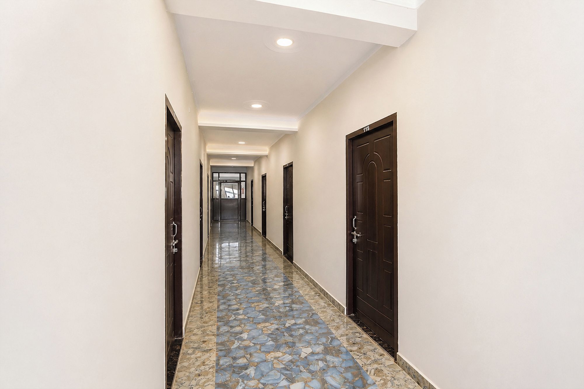 Um corredor com portas em ambos os lados, piso de azulejos e teto com iluminação embutida.
