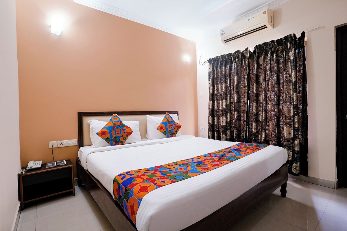 Quarto de hotel com cama, telefone de apoio e janela com cortinas estampadas.