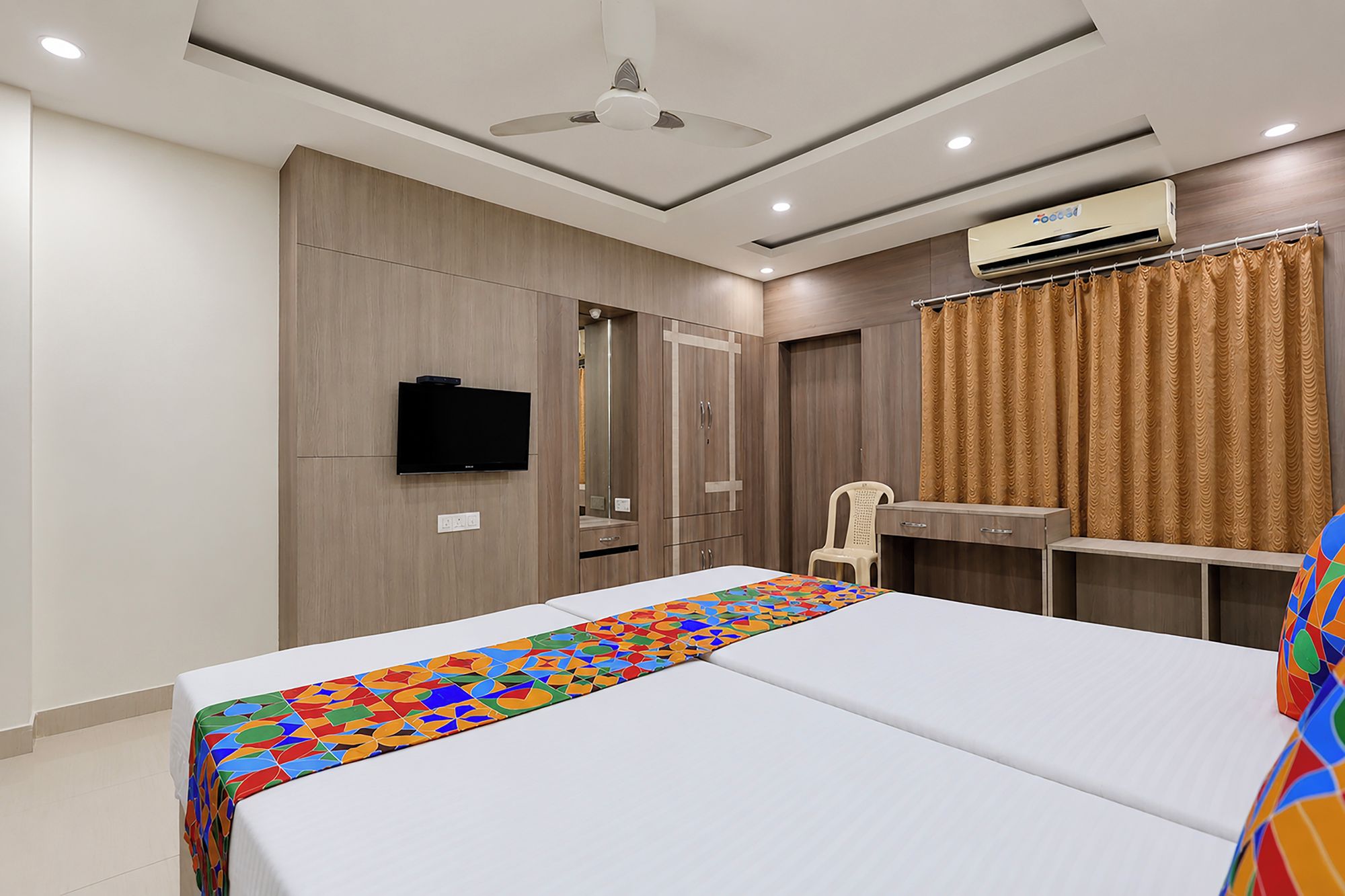 Quarto de hotel com cama, escrivaninha, cadeira, televisão e ar condicionado.