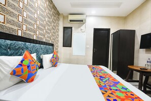 Quarto de hotel com parede estampada, cama com almofadas coloridas, televisão de tela plana e minibar.
