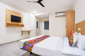 Quarto de hotel com cama, televisão na parede, aparelho de ar condicionado e ventoinha no teto.