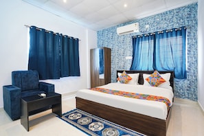 Quarto com cama, mesa de cabeceira, cadeira, guarda-roupa e tapete estampado.