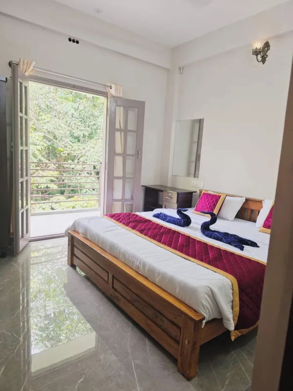 Quarto com cama, escrivaninha, espelho e porta de vidro deslizante para área externa.