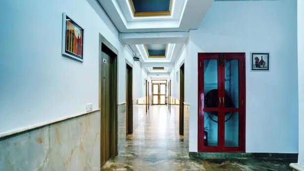 Um corredor com piso de mármore, portas à esquerda e uma porta vermelha à direita.
