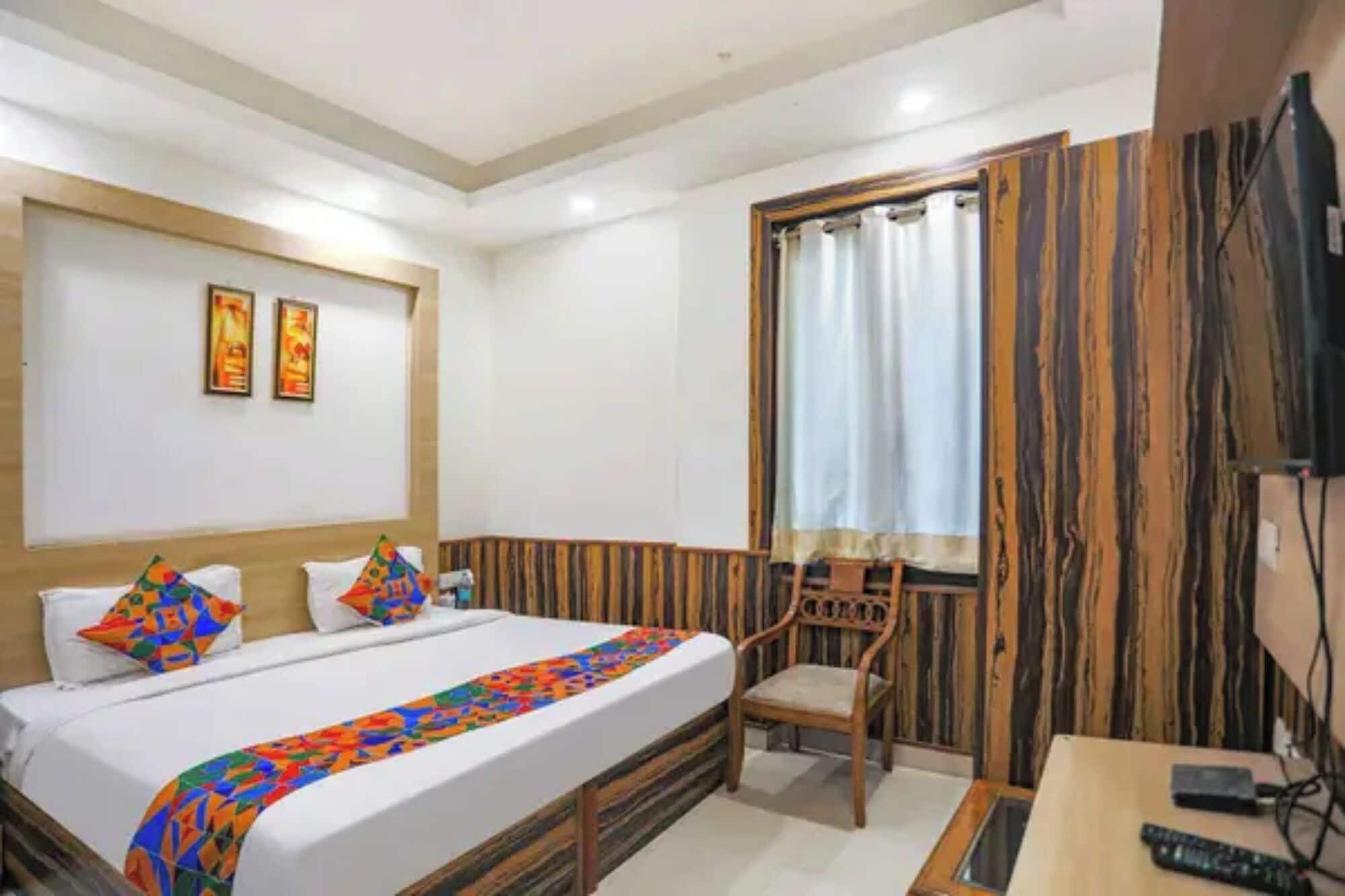Quarto de hotel com cama, cadeira, televisão e janela com cortinas.