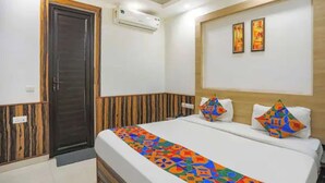 Quarto de hotel com cama, porta, aparelho de ar condicionado e duas fotos emolduradas na parede.