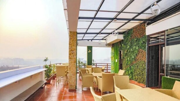 Terraço no telhado com móveis de vime, teto de vidro e parede verde com plantas.