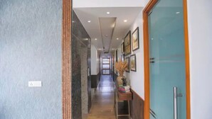 Corredor com parede de mármore, porta de madeira e uma pequena mesa com livros e um vaso.