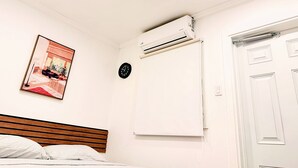 Um quarto com uma cama, um aparelho de ar condicionado, um relógio e uma porta.
