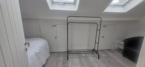Quarto com claraboia, uma cama, guarda-roupa e uma cadeira preta.