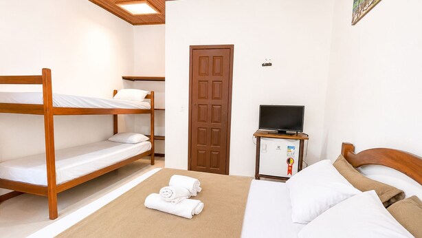 Quarto de hotel com beliches, uma televisão sobre uma mesinha e uma porta.