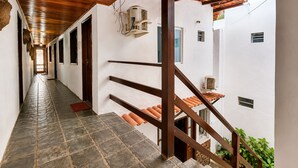 Um corredor com piso ladrilhado, teto de madeira e escada com corrimão.