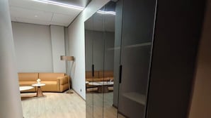 Quarto moderno com piso de madeira, sofá, mesa de centro e armário com espelho.