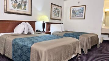 Quarto de hotel com duas camas, mesa de cabeceira com abajur e obras de arte botânicas emolduradas nas paredes.
