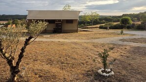 Um edifício térreo com telhado plano, cercado por grama seca e vegetação rala, sob um céu parcialmente nublado.
