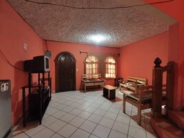 Quarto com piso de azulejos, porta de madeira, televisão sobre um suporte e dois bancos de madeira.