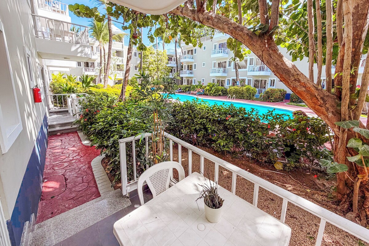 Varanda com vista para uma piscina, rodeada por vegetação e um guarda-corpo branco.