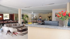 Uma área de recepção de hotel com balcão, espaço para sentar e um bar ao fundo.