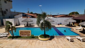 Uma piscina com deck ladrilhado, rodeada por espreguiçadeiras e guarda-sóis.