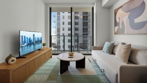 Uma sala de estar moderna com uma televisão grande, uma mesa de centro redonda, um sofá e uma varanda com vista para a cidade.