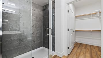 Um banheiro moderno com chuveiro em cabine de vidro, banheira branca e piso de madeira.
