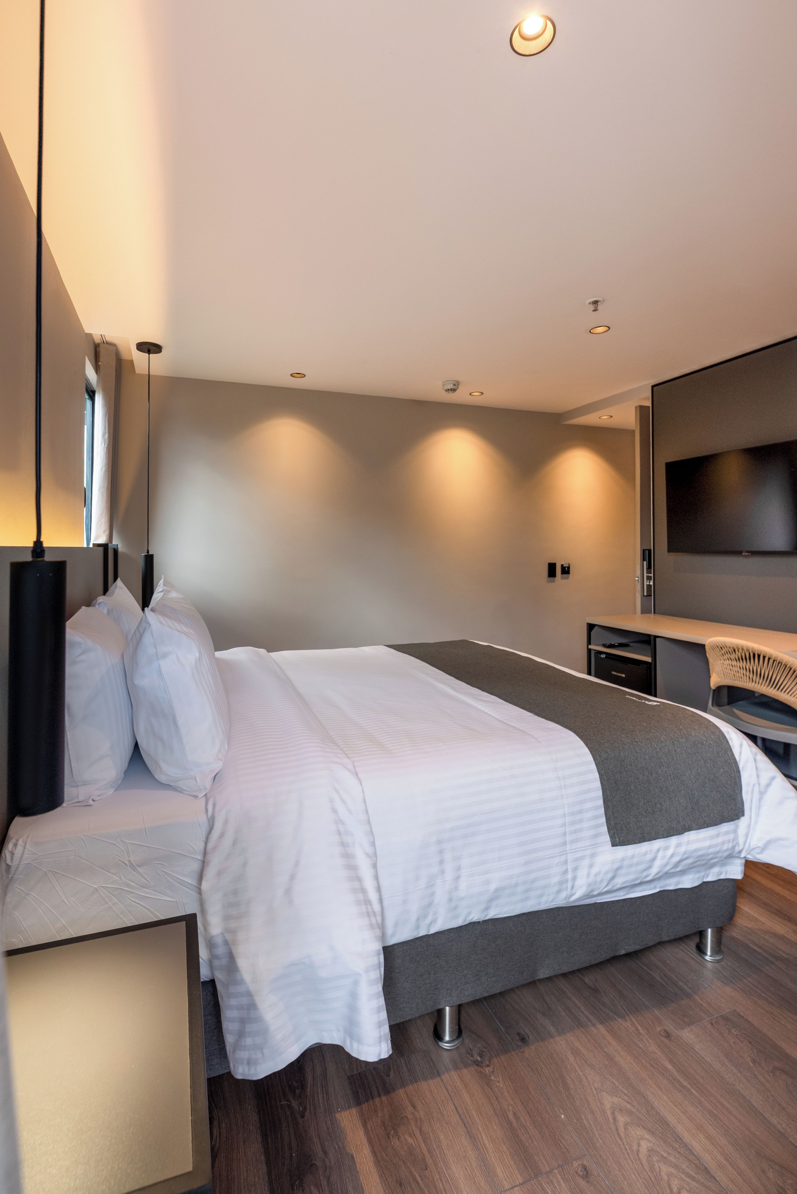 Quarto de hotel moderno com cama grande, escrivaninha e TV de tela plana.