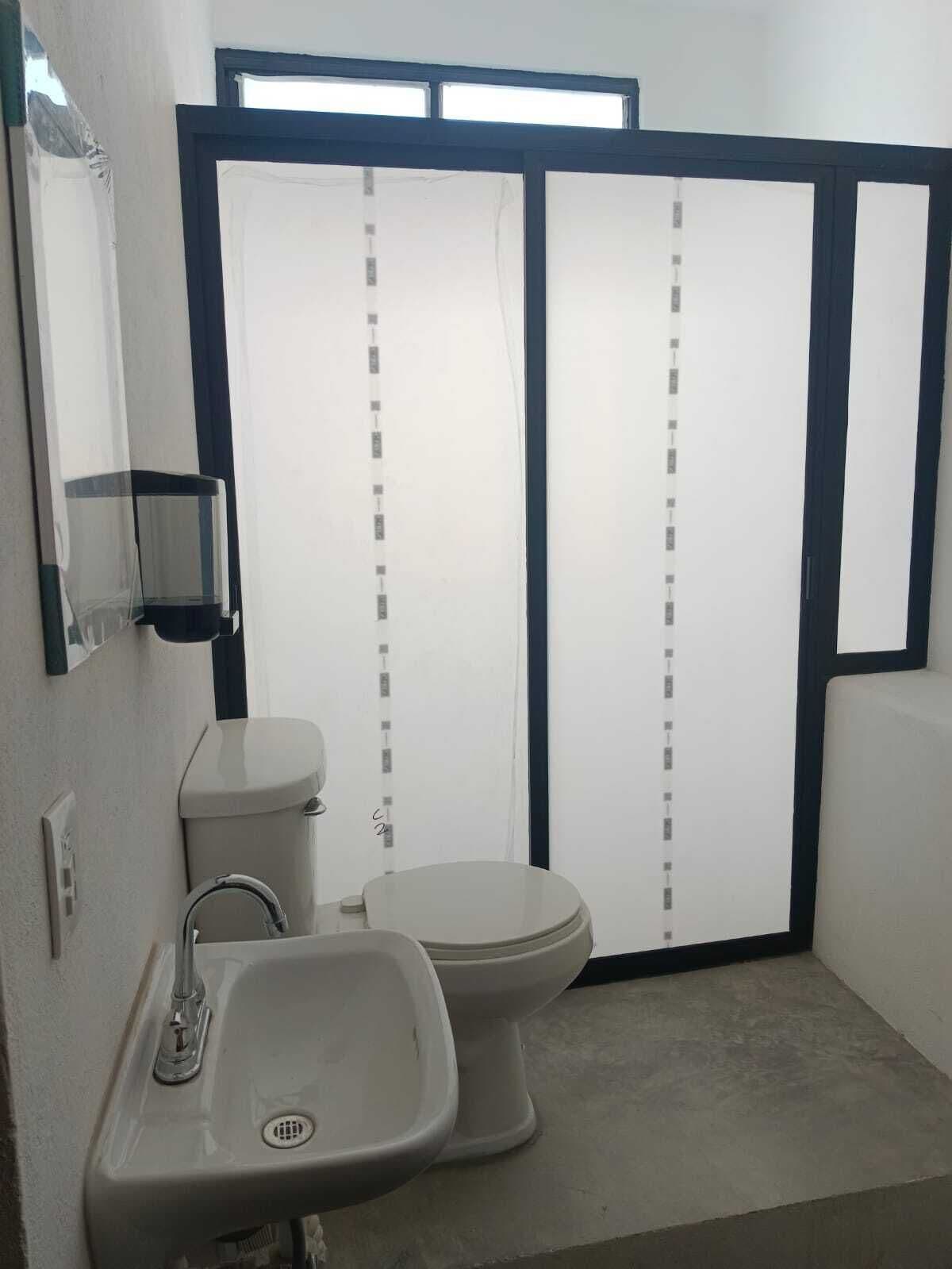 Casa de banho com sanita, lavatório e zona de duche com porta de vidro jateado.