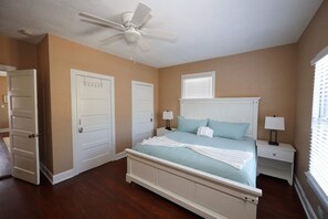Quarto com cama, mesas de cabeceira, ventilador de teto e janela com persianas.