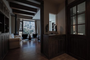 Quarto com piso de madeira, sofá branco, armário de madeira e uma janela grande com vista para uma área arborizada.