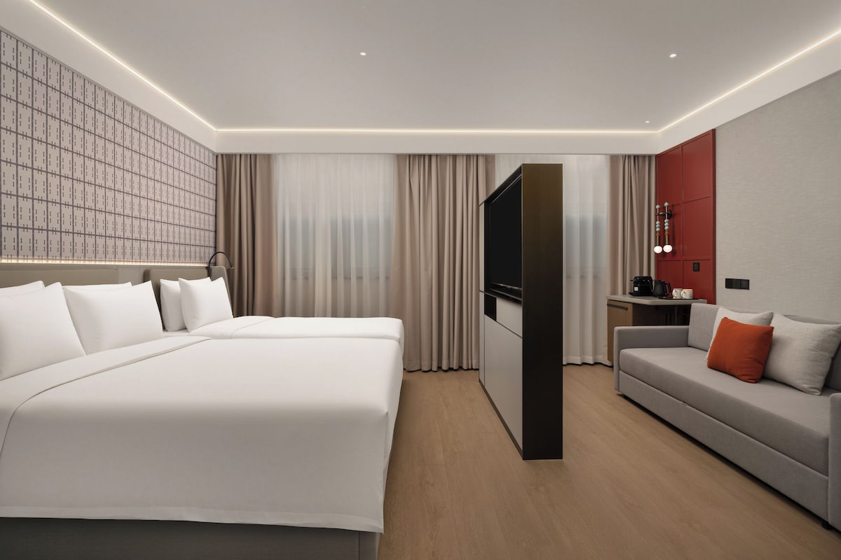 Quarto de hotel com cama grande, sofá, televisão e minibar.