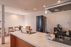 Uma cozinha moderna com ilha central, eletrodomésticos de aço inoxidável e um espaço de estar com cadeiras de madeira.