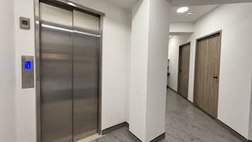 Um elevador moderno com visor digital, corredor com portas de madeira e soalho claro.