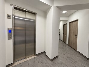 Um elevador moderno com visor digital, corredor com portas de madeira e soalho claro.