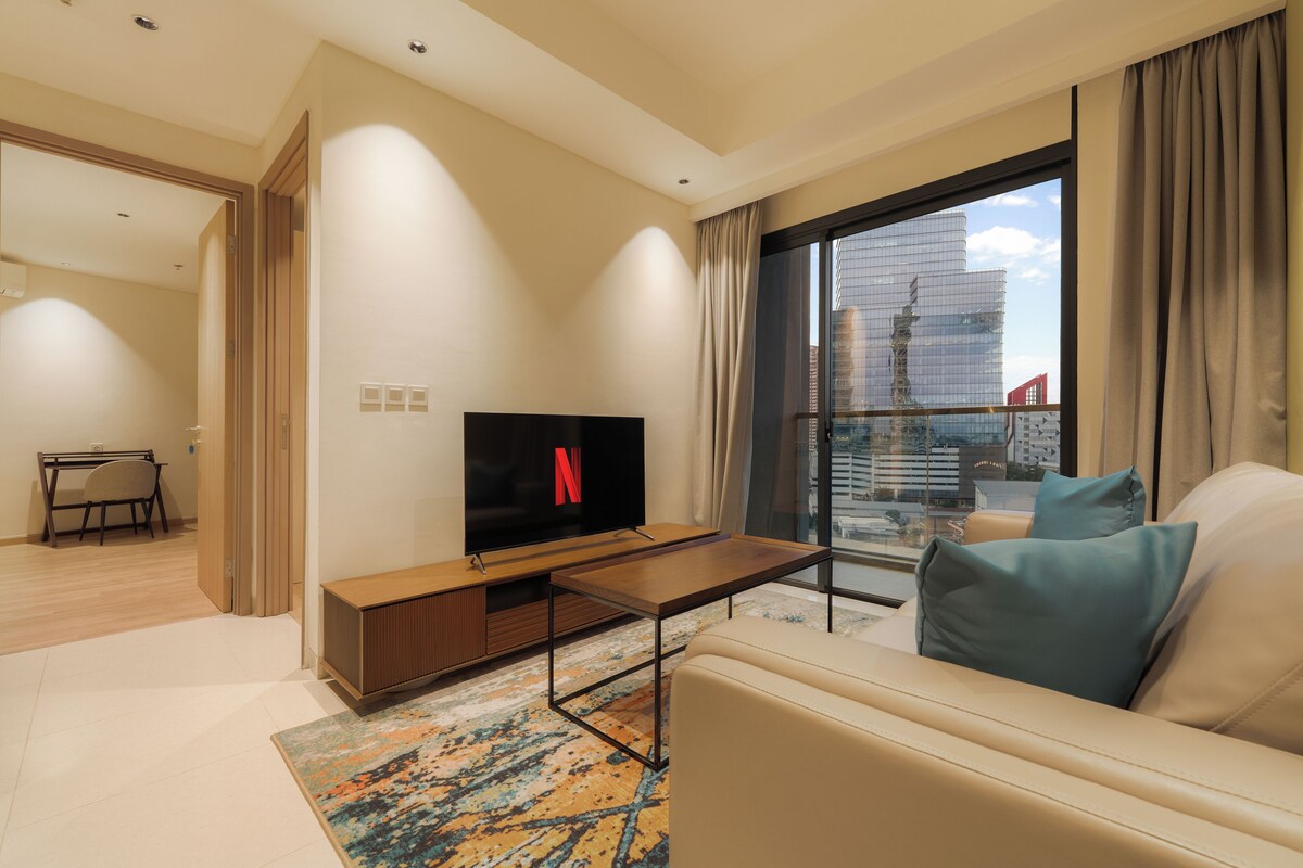 Uma sala de estar moderna com televisão de tela plana, sofá, mesa de centro e vista para a cidade através de uma grande janela.