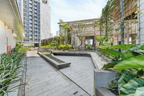 Um pátio urbano moderno com um caminho pavimentado, vasos com diversas plantas e um edifício com fachada de vidro.