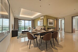 Uma área de jantar moderna com uma mesa grande posta para quatro pessoas, um sofá e vista para a cidade através de janelas amplas.