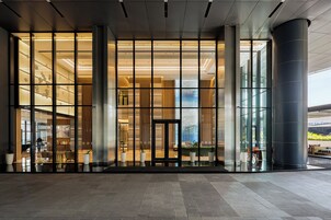 Entrada de um edifício moderno com grandes portas de vidro, um balcão de recepção e vista para o interior.