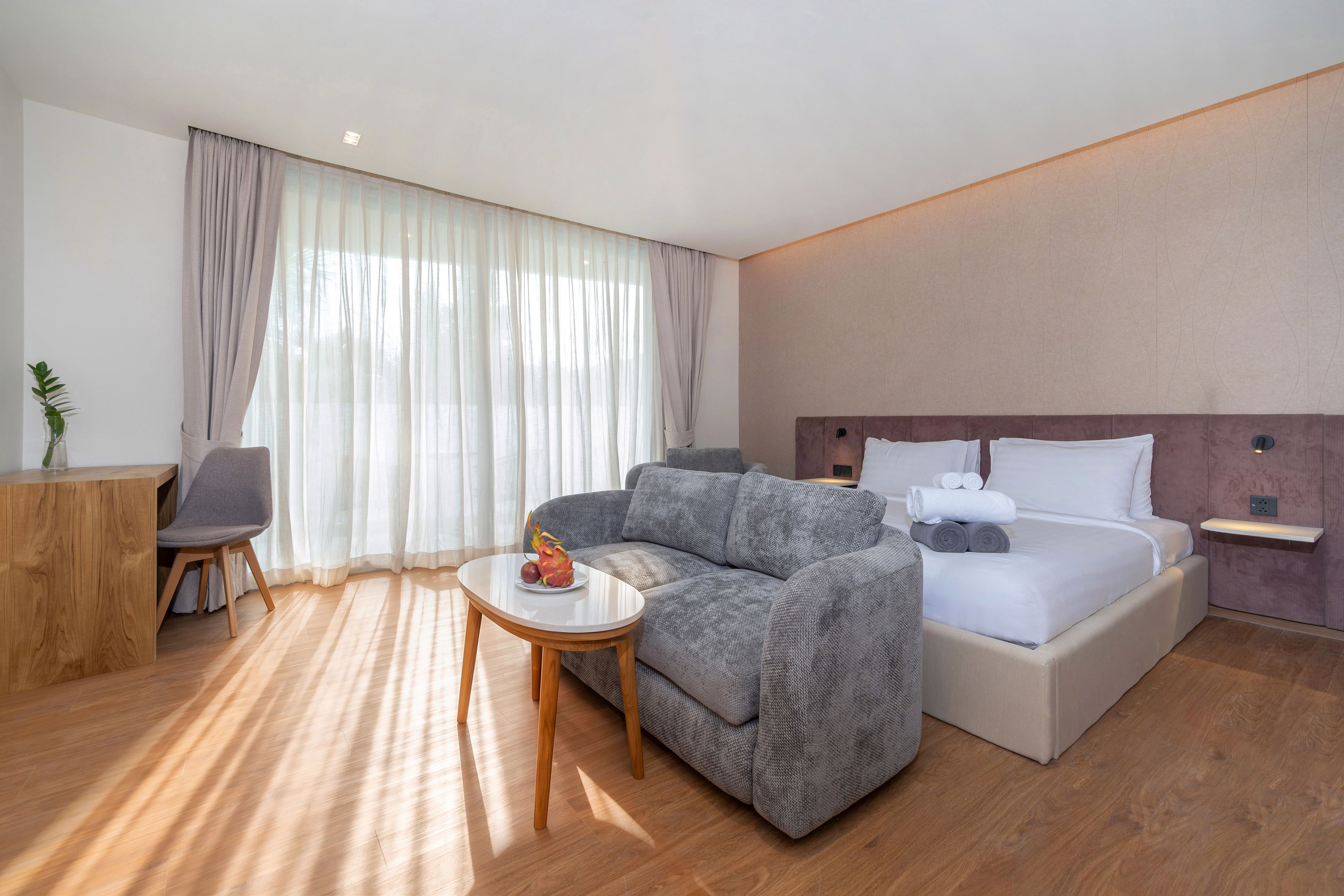 Quarto de hotel com cama, sofá, mesinha e escrivaninha.