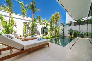 Uma área moderna de piscina ao ar livre com espreguiçadeiras e plantas tropicais.