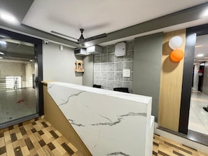 Uma área de recepção com balcão de mármore, ventilador de teto e parede revestida de azulejos.