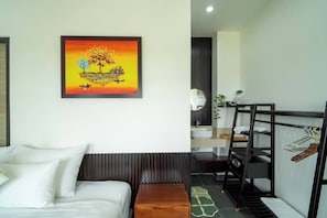 Quarto de hotel com cama, um banquinho de madeira, uma pintura, banheiro com pia e espelho, e um sapateiro.