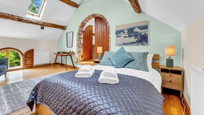 Quarto com cama grande, teto de madeira, vista para o verde e um quadro na parede.